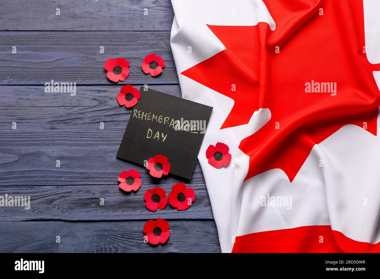 Poppy flowers with flags of Canada and card on blue wooden background ...