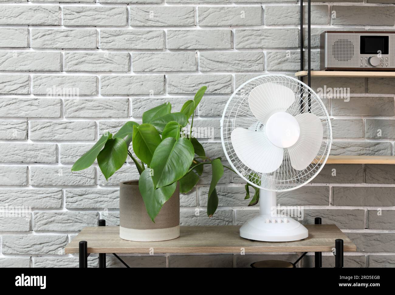 Electric fan with houseplant on shelf near grey brick wall in room ...