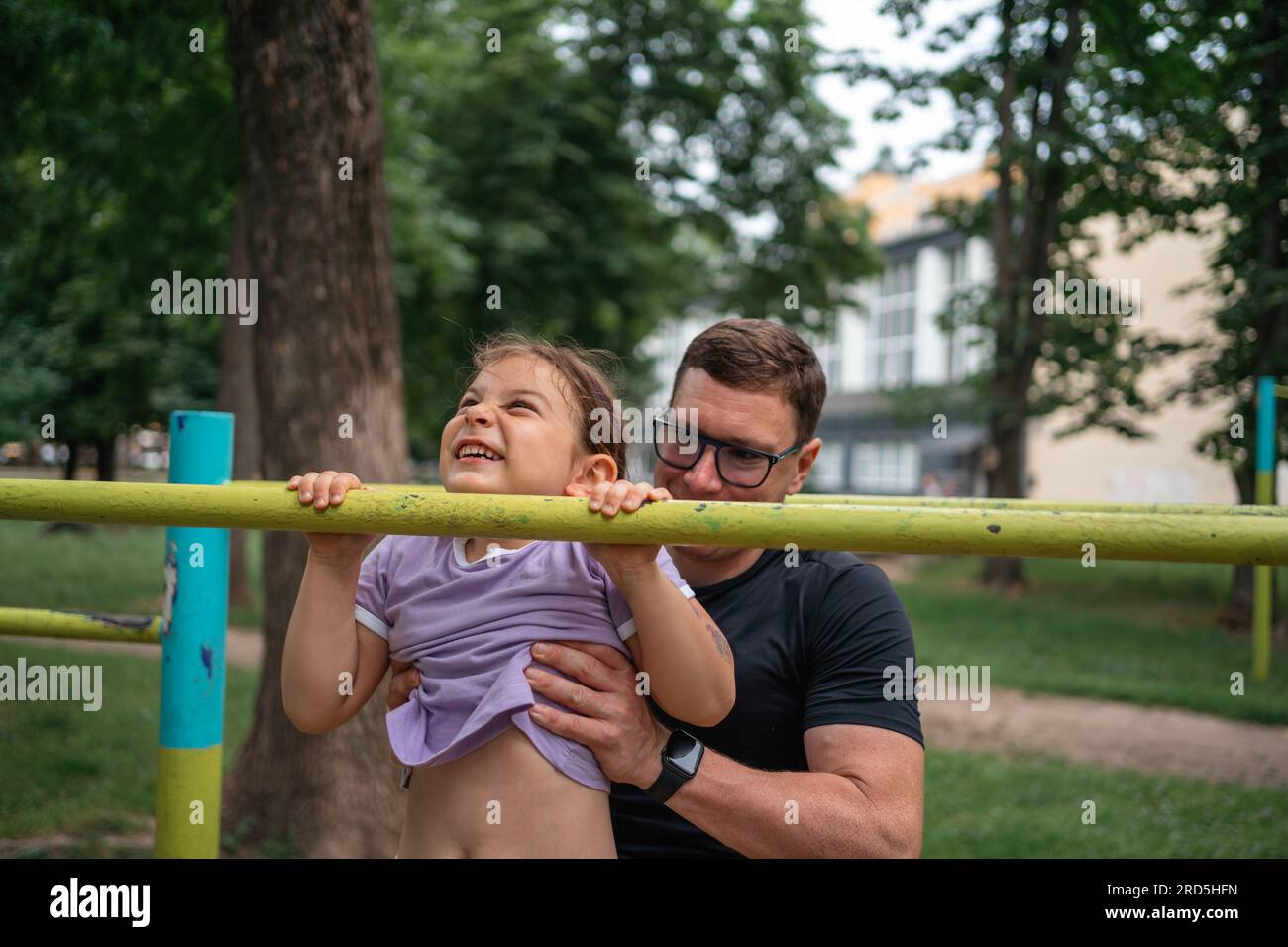 Father with child girl doing pull-ups on workout outdoor area. Healthy ...