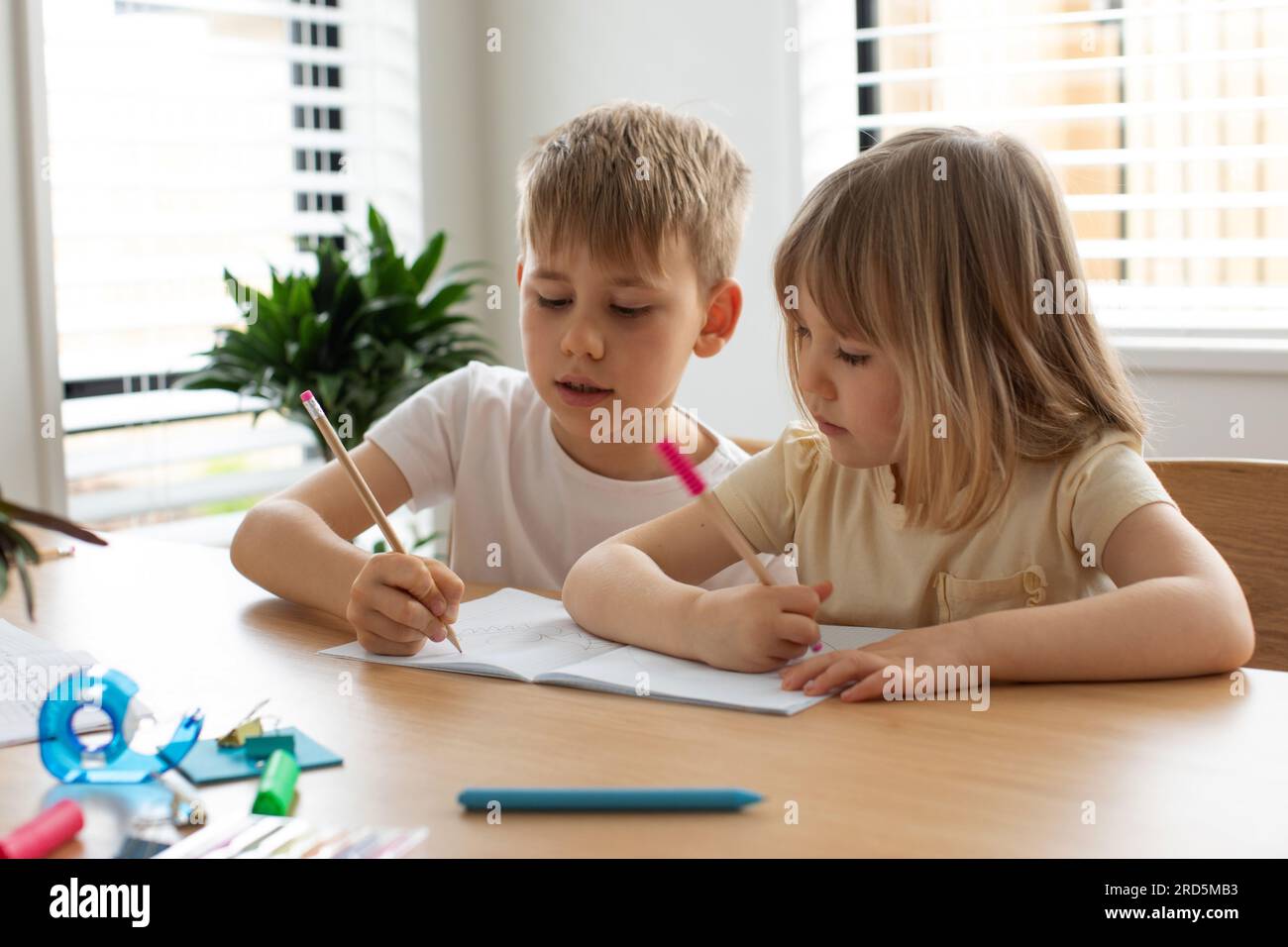 Brother and sister write and draw together with pencils at the table ...