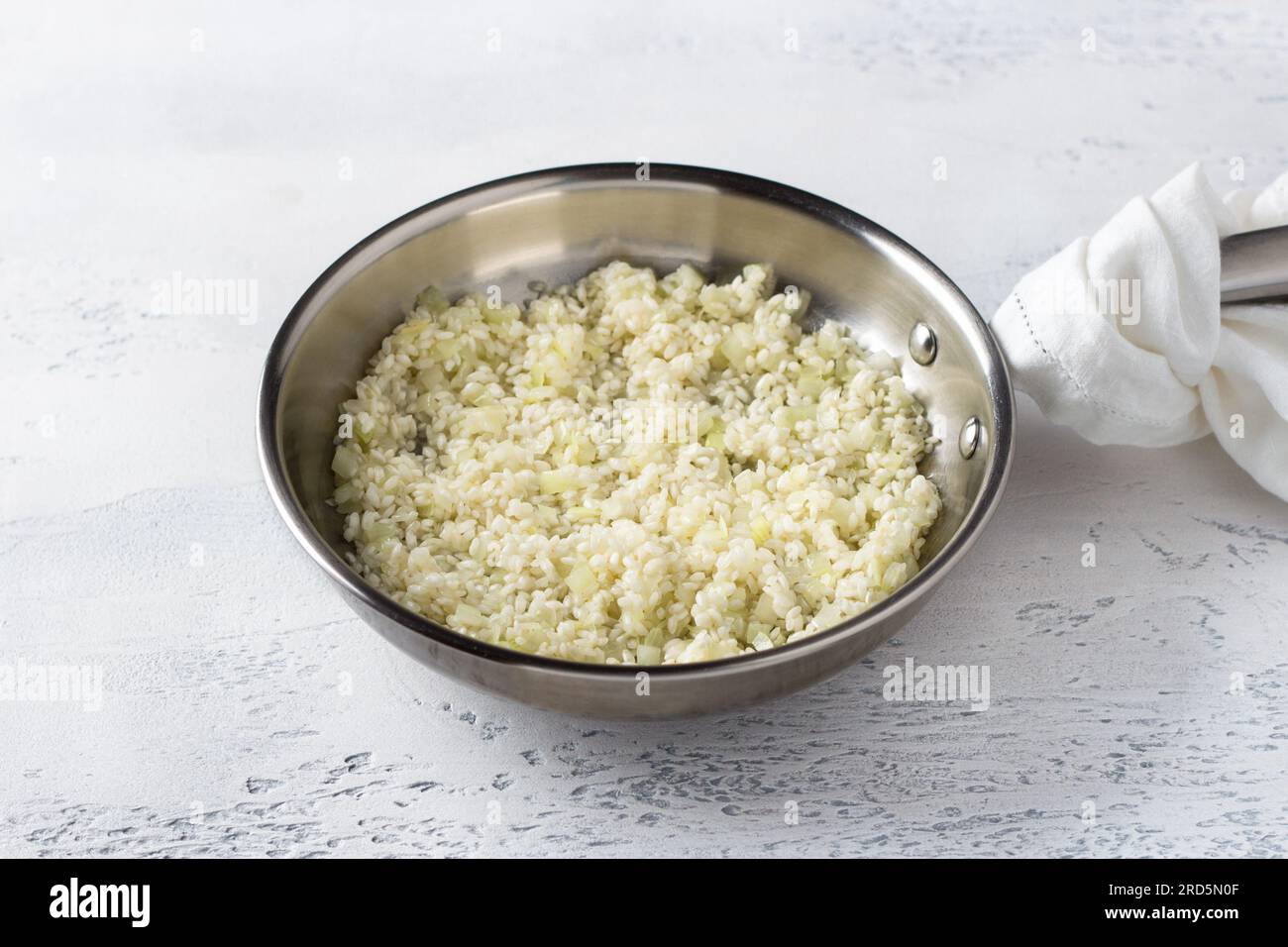 Frying pan with uncooked rice and onions on a light blue background ...