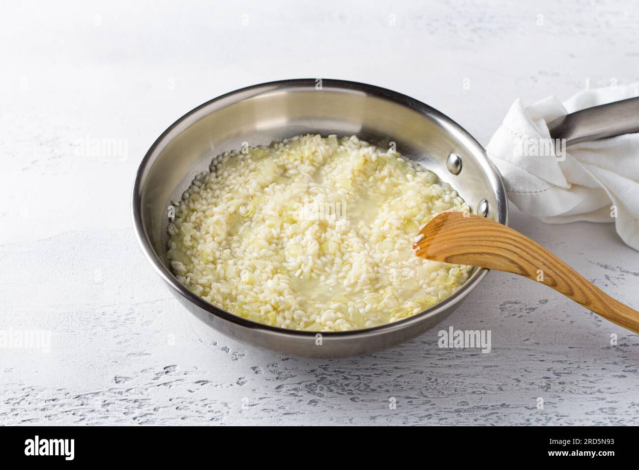 Frying pan with arborio rice, onion and broth on a light blue ...