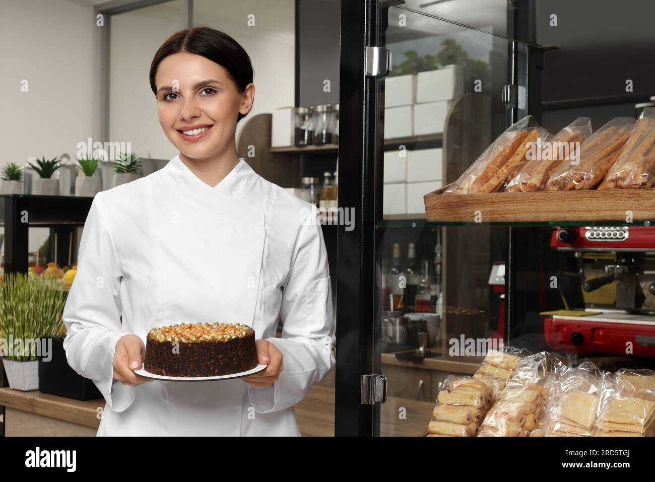 Happy baker presenting delicious cake near showcase with pastries in ...