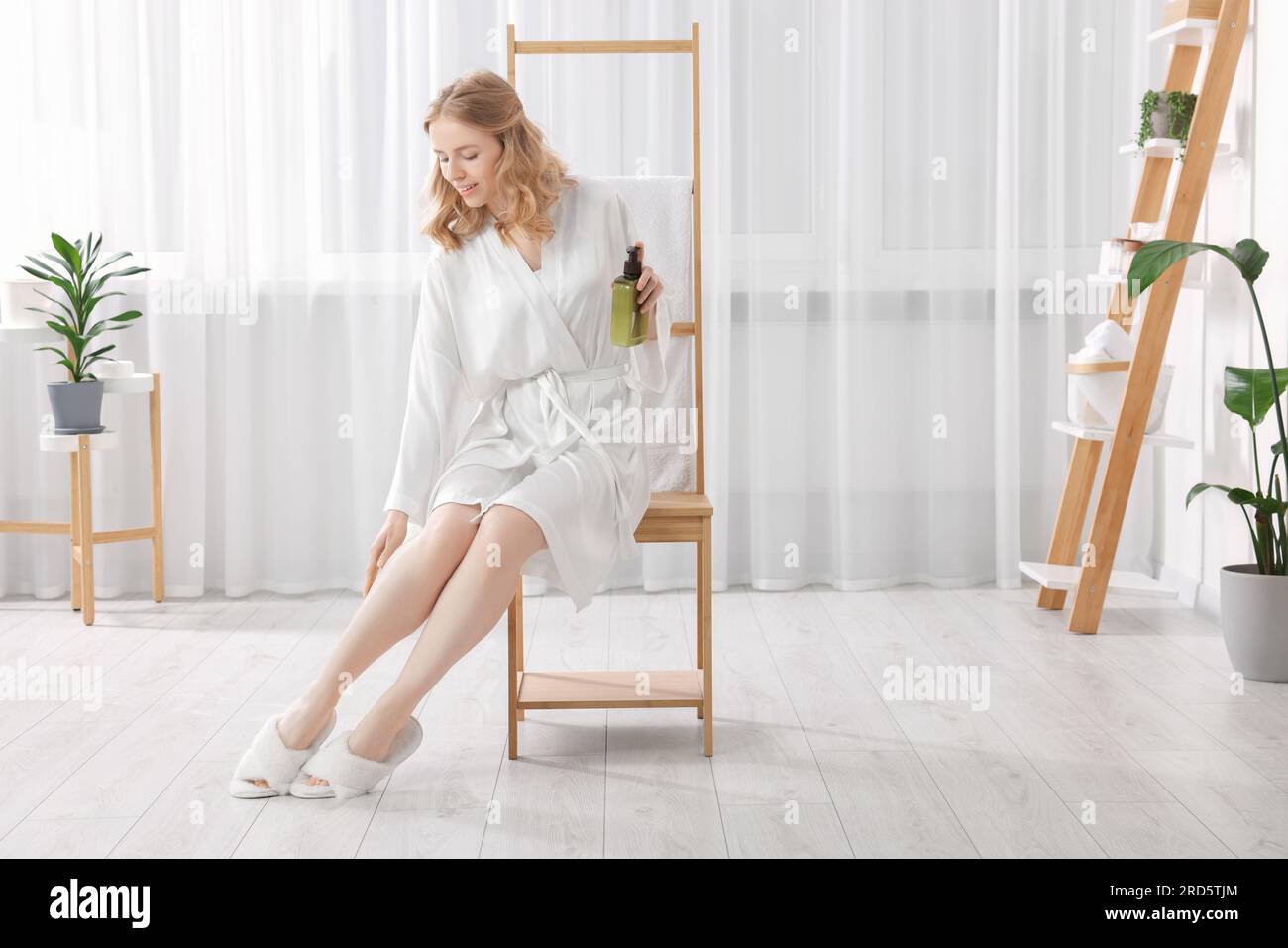 Beautiful young woman applying oil onto leg indoors Stock Photo - Alamy