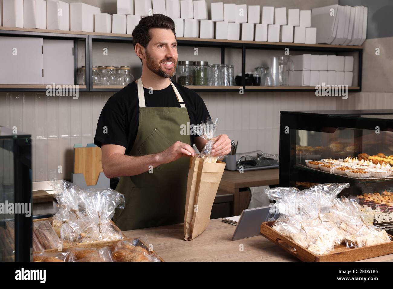 Happy seller putting pastry into paper bag at cashier desk in bakery ...