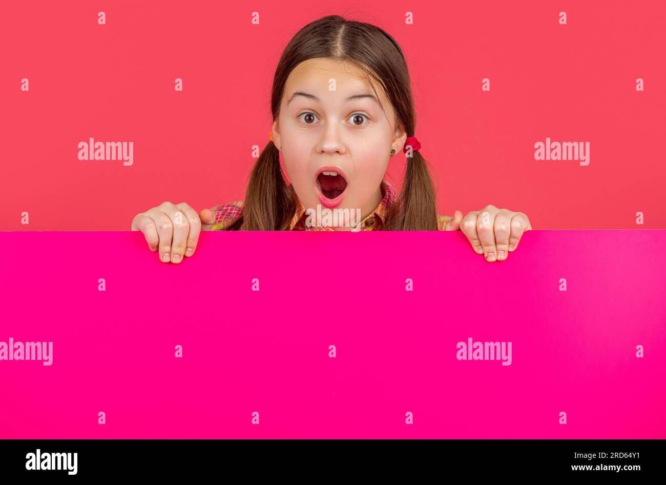 amazed kid behind blank pink paper with copy space for advertisement ...