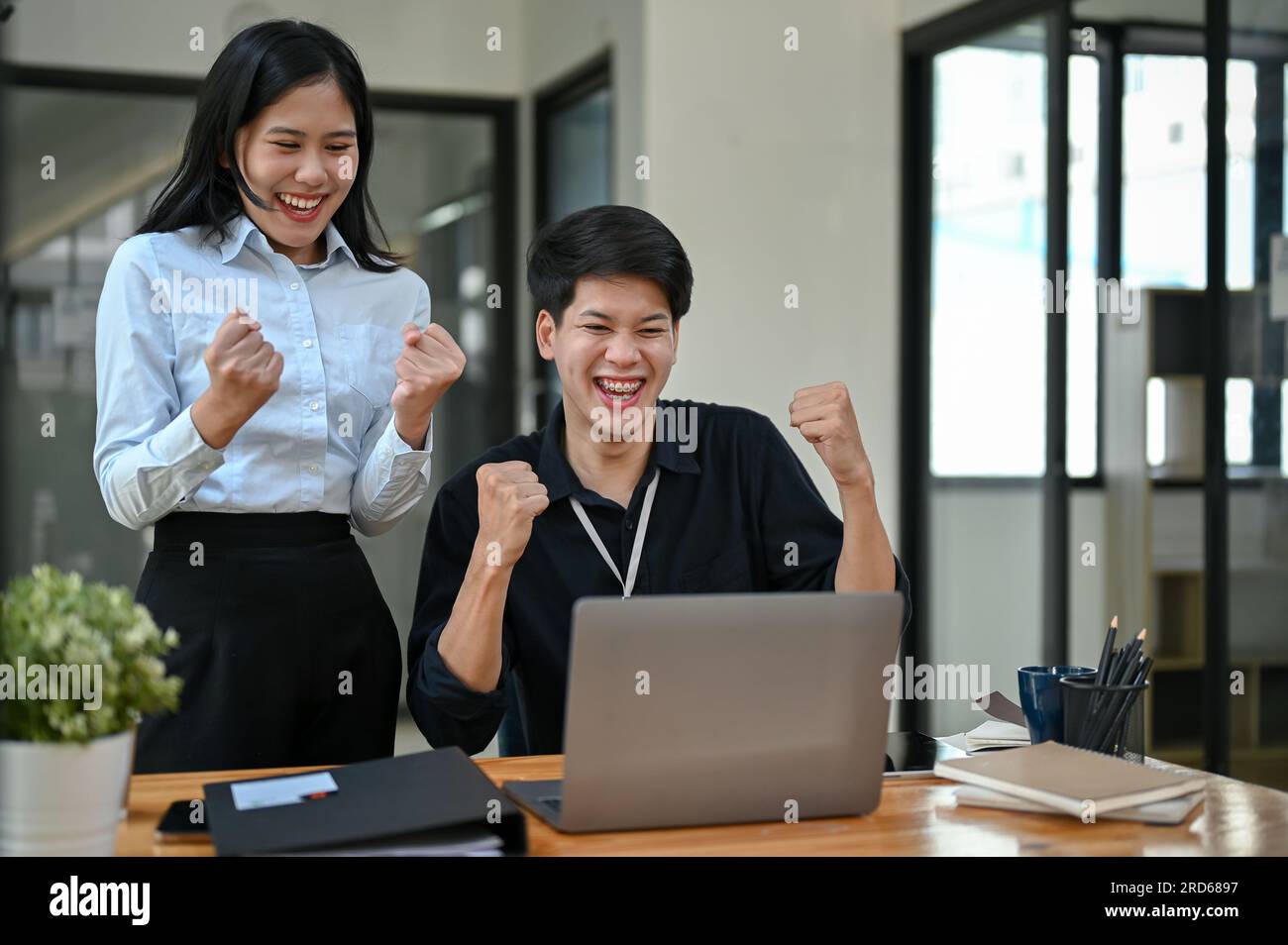 Two cheerful and overjoyed Asian office workers are celebrating their ...