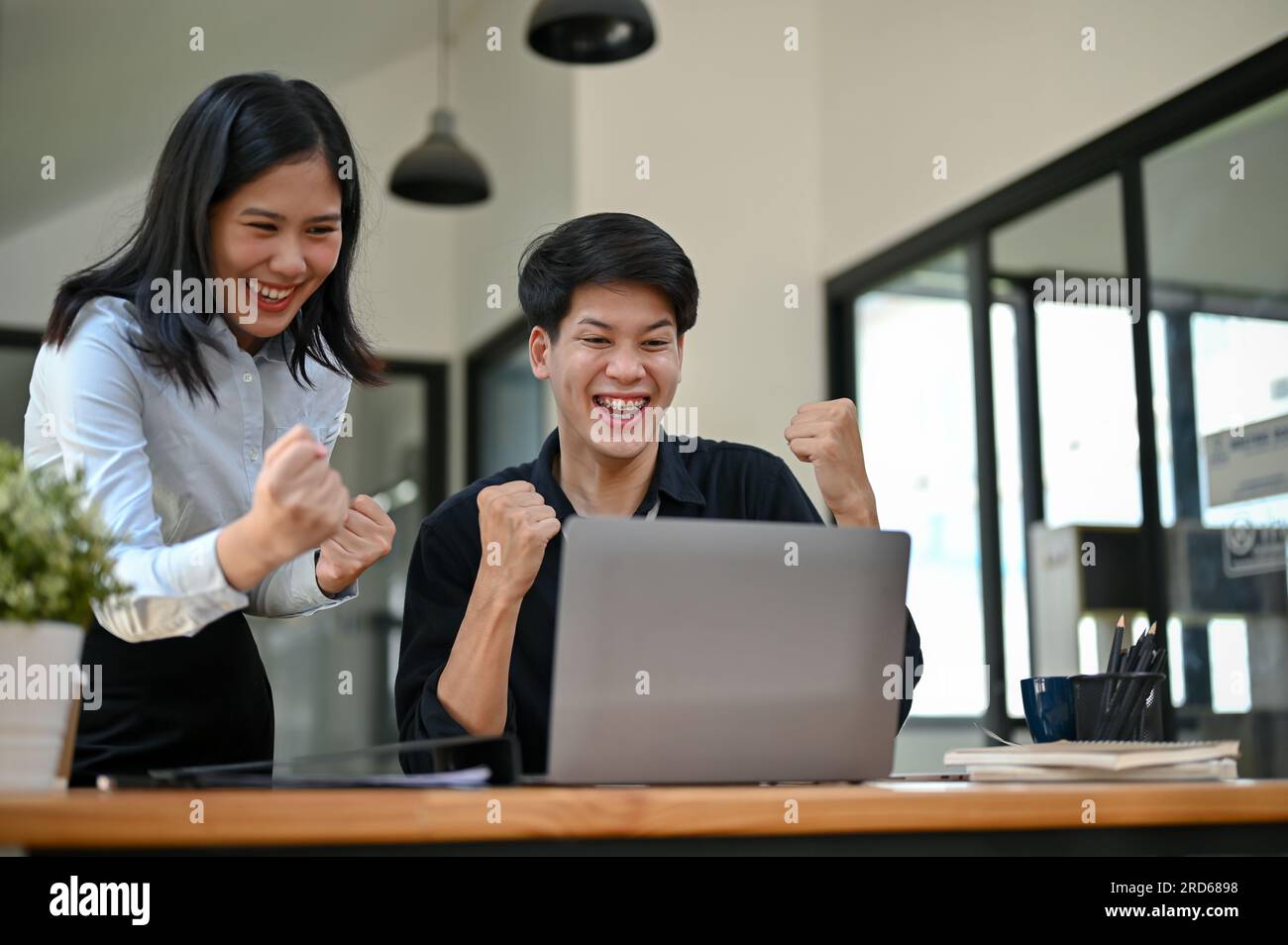 Two cheerful and overjoyed Asian office workers are celebrating their ...