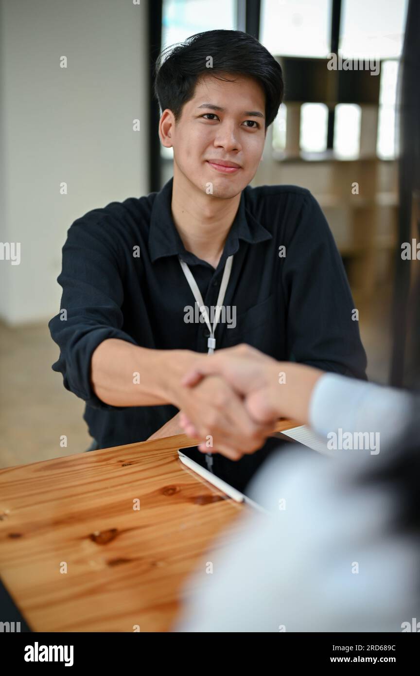 A portrait of a handsome young Asian office worker shaking hands with a ...