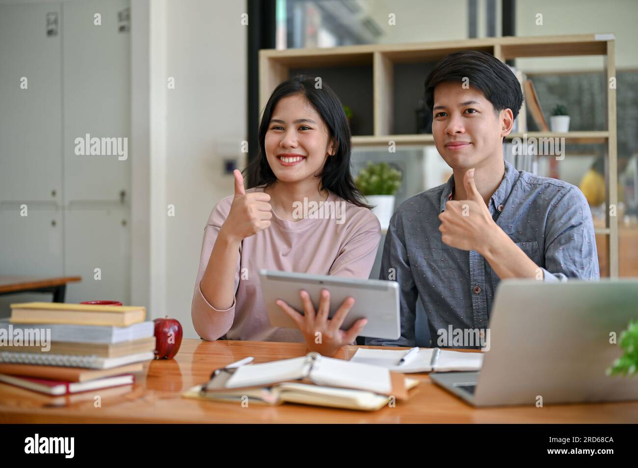 Two Asian college students are showing their thumbs up while studying at a tutorial school ...