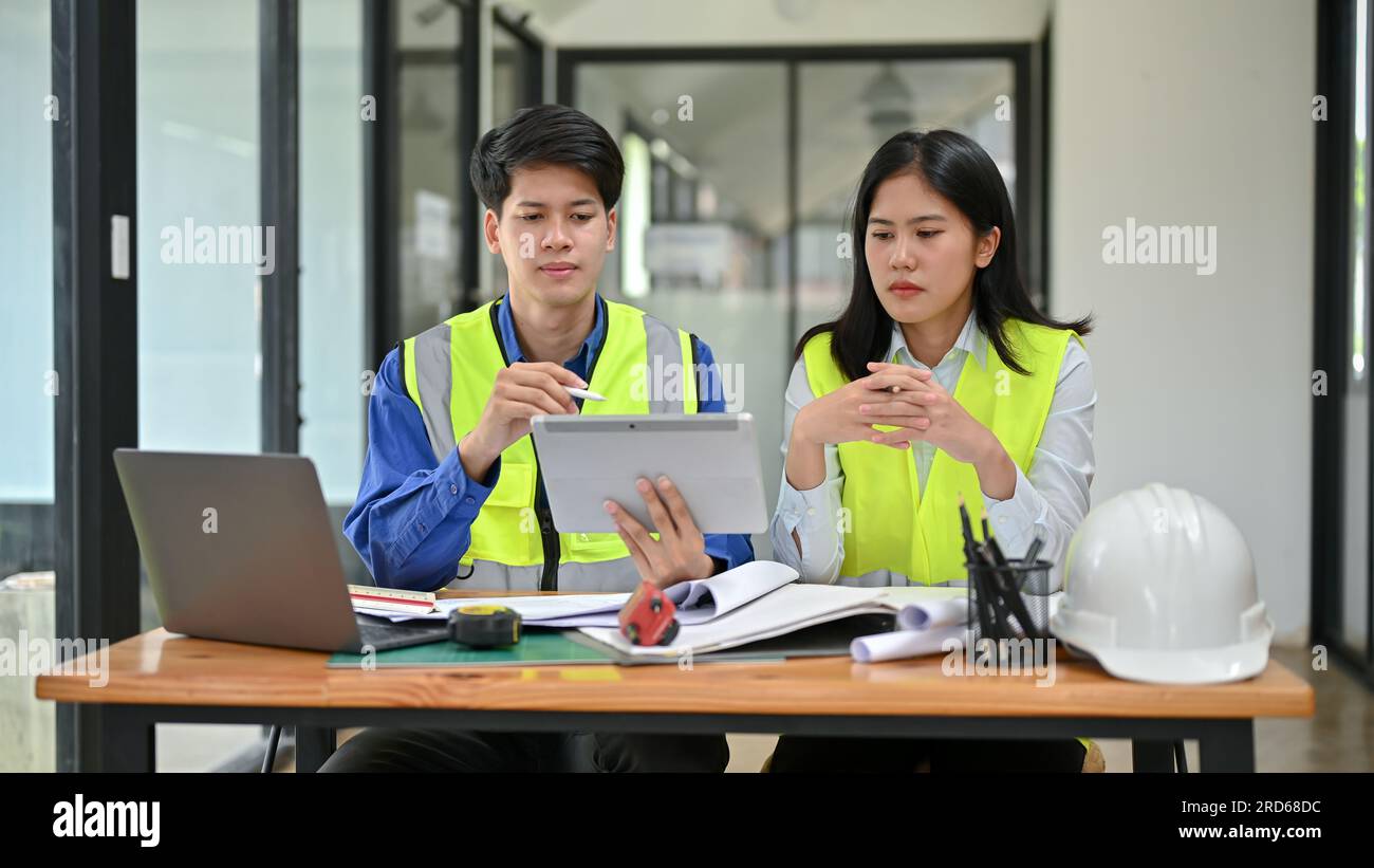 Two professional and serious Asian engineers wearing safety vests are ...