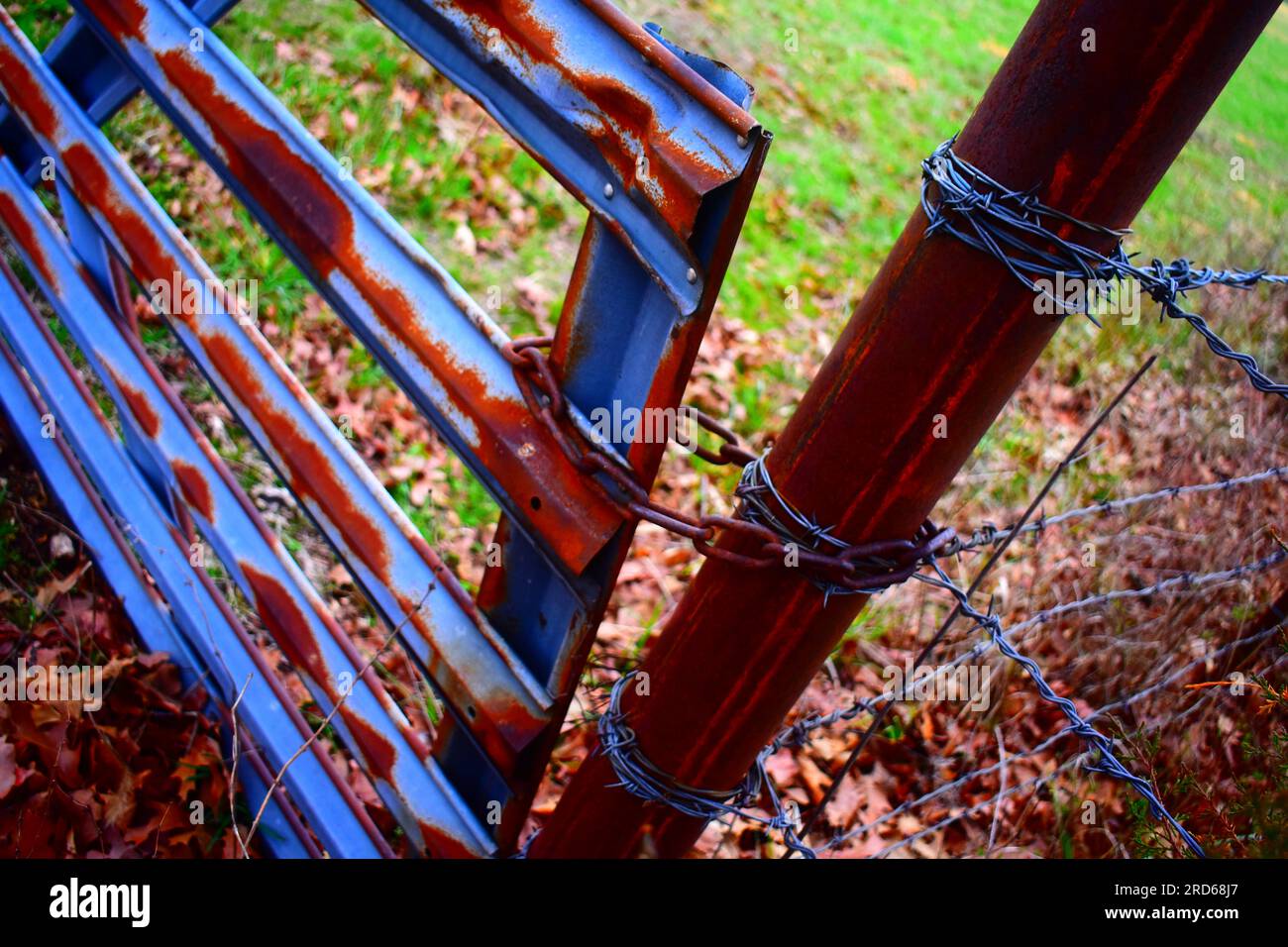 Old metal gate held closed by a chain connected to a rusty metal post ...