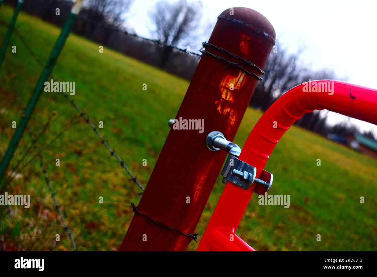 A bright red metal gate attached to a rusty metal fence post makes an ...
