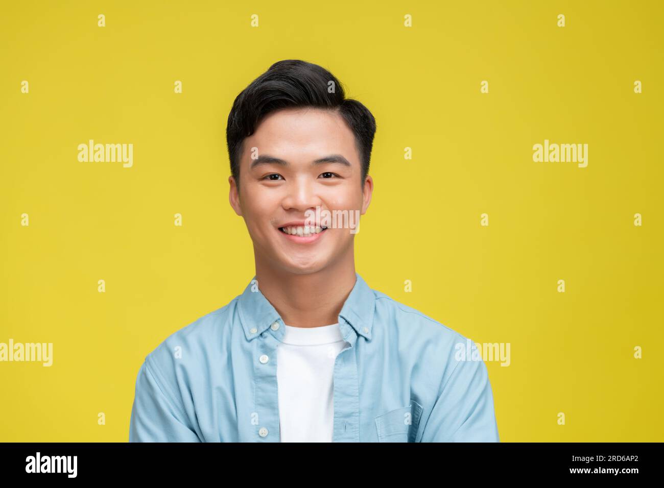 Happy asian guy smiling while using mobile phone isolated over yellow ...