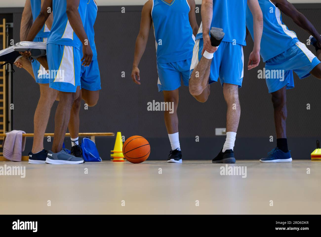 Diverse male basketball players stretching and warming up at gym, copy ...