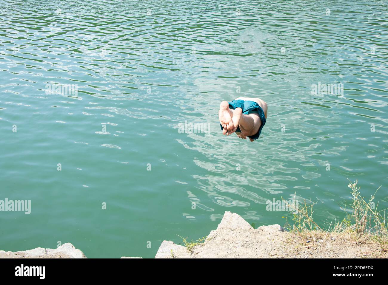 A guy in a jump before diving into a quarry with water in the summer in ...