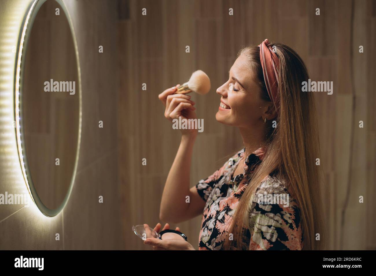 Smiling blonde girl doing makeup on in front of the mirror Stock Photo ...