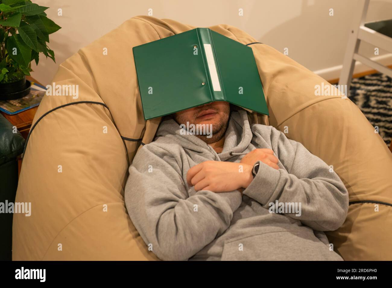 Young man lying on bean bag, face covered by green folder. Taking a ...