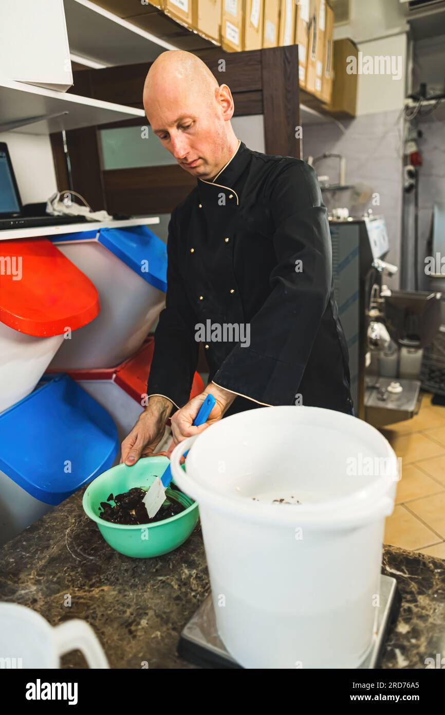 Vertical shot of pastry chef in black uniform mixing batter with ...