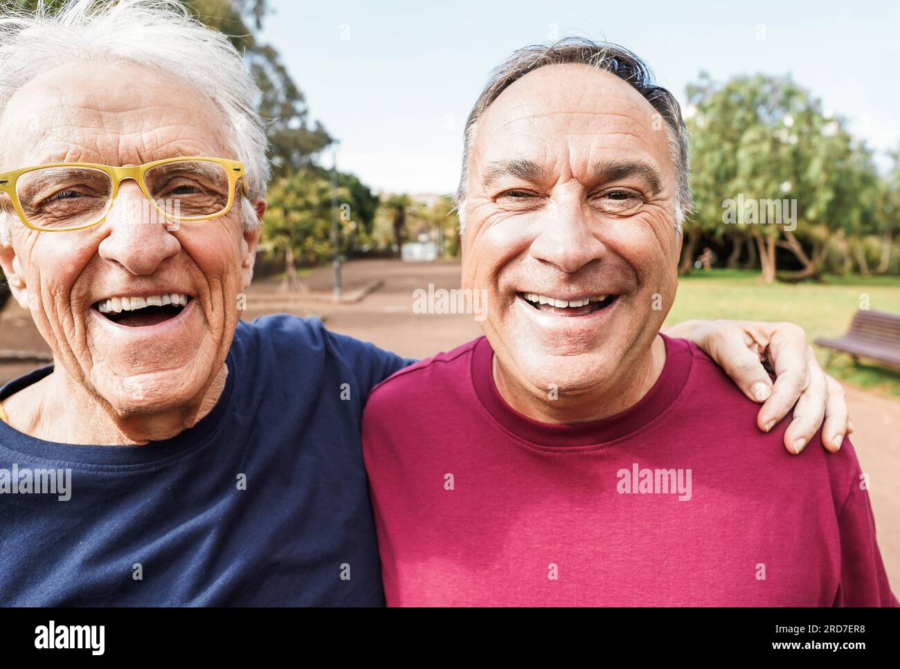 Two male senior friends having fun during workout running at city park ...
