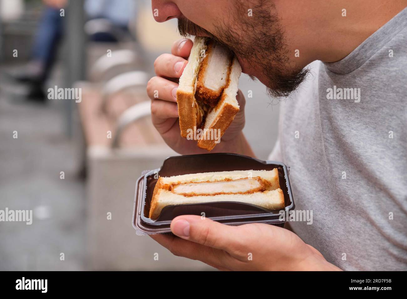 Unrecognizable man eating katsu sando at street Stock Photo - Alamy