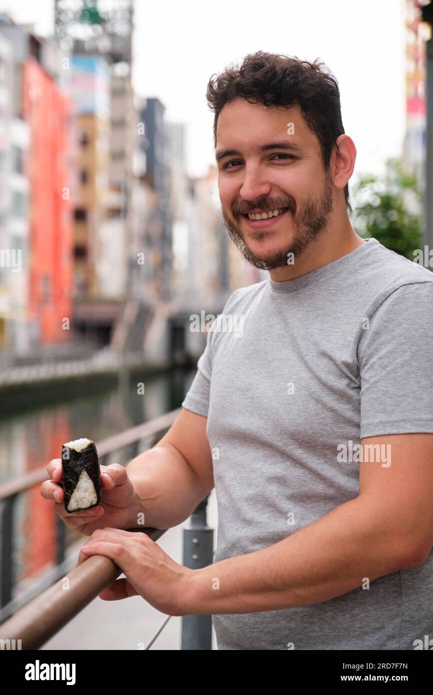Tourist eating onigiri and looking at camera at street Stock Photo - Alamy