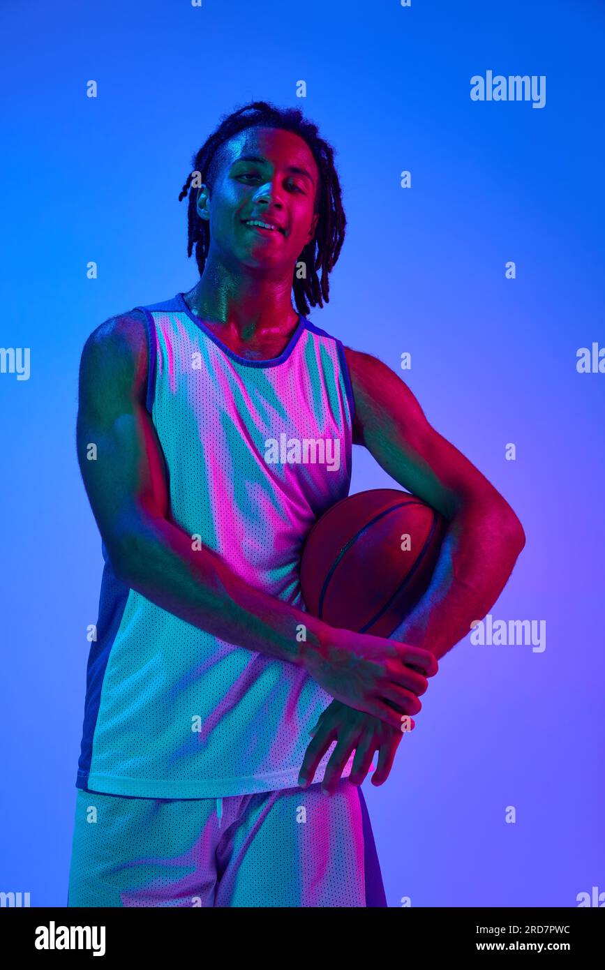 Young man with dreads, basketball player in uniforma posing with ball ...