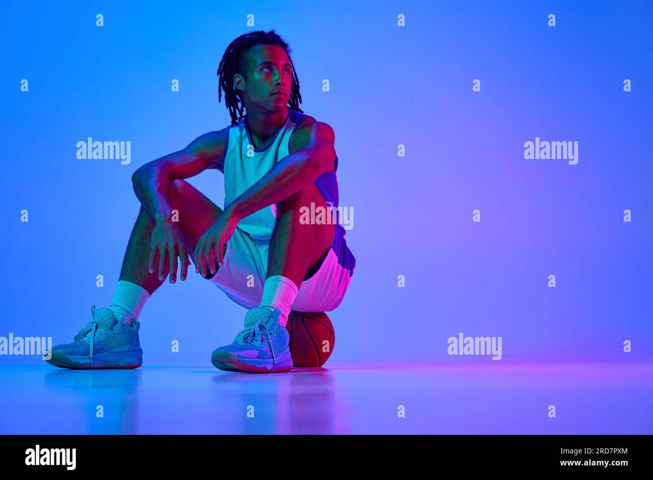 Portrait of young guy, basketball player in uniform, sitting on floor ...