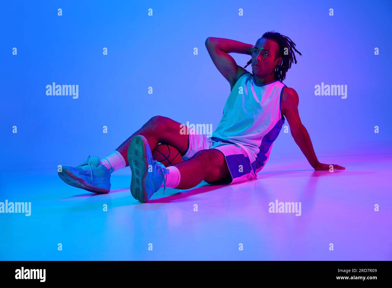 Portrait of young guy, basketball player in uniform, sitting on floor ...