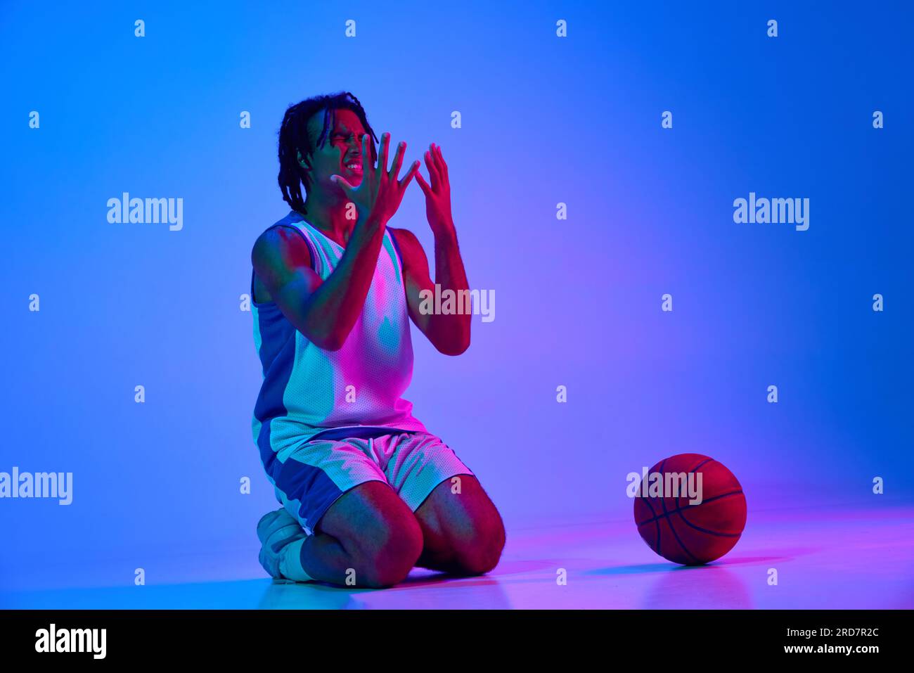 Loosing game. Young guy, basketball player sitting on knees in sadness ...