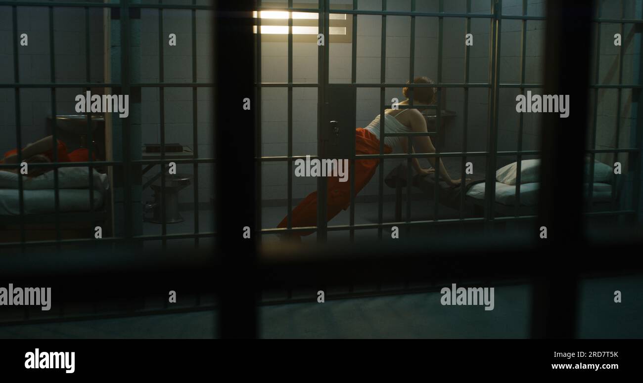 One female prisoner in orange uniform lies on the bed, another boxing in prison cell. Women ...