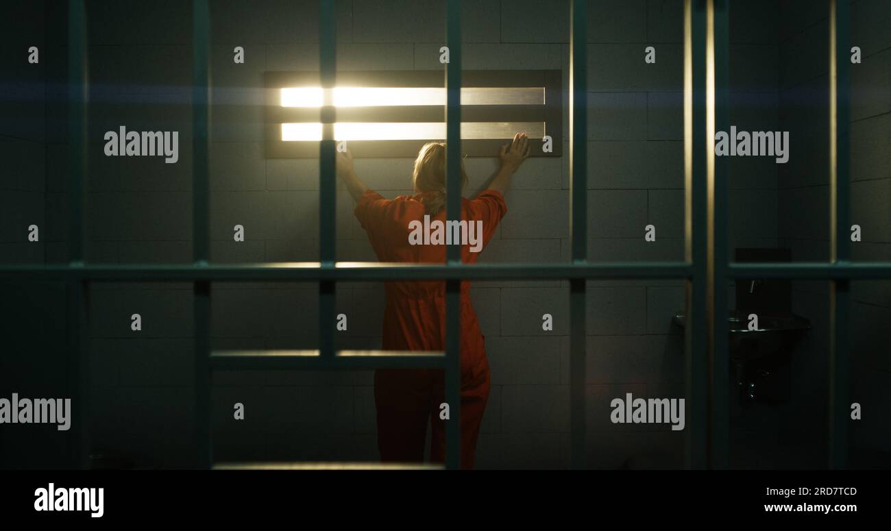 Female prisoner in orange uniform walks and stands behind metal bars ...