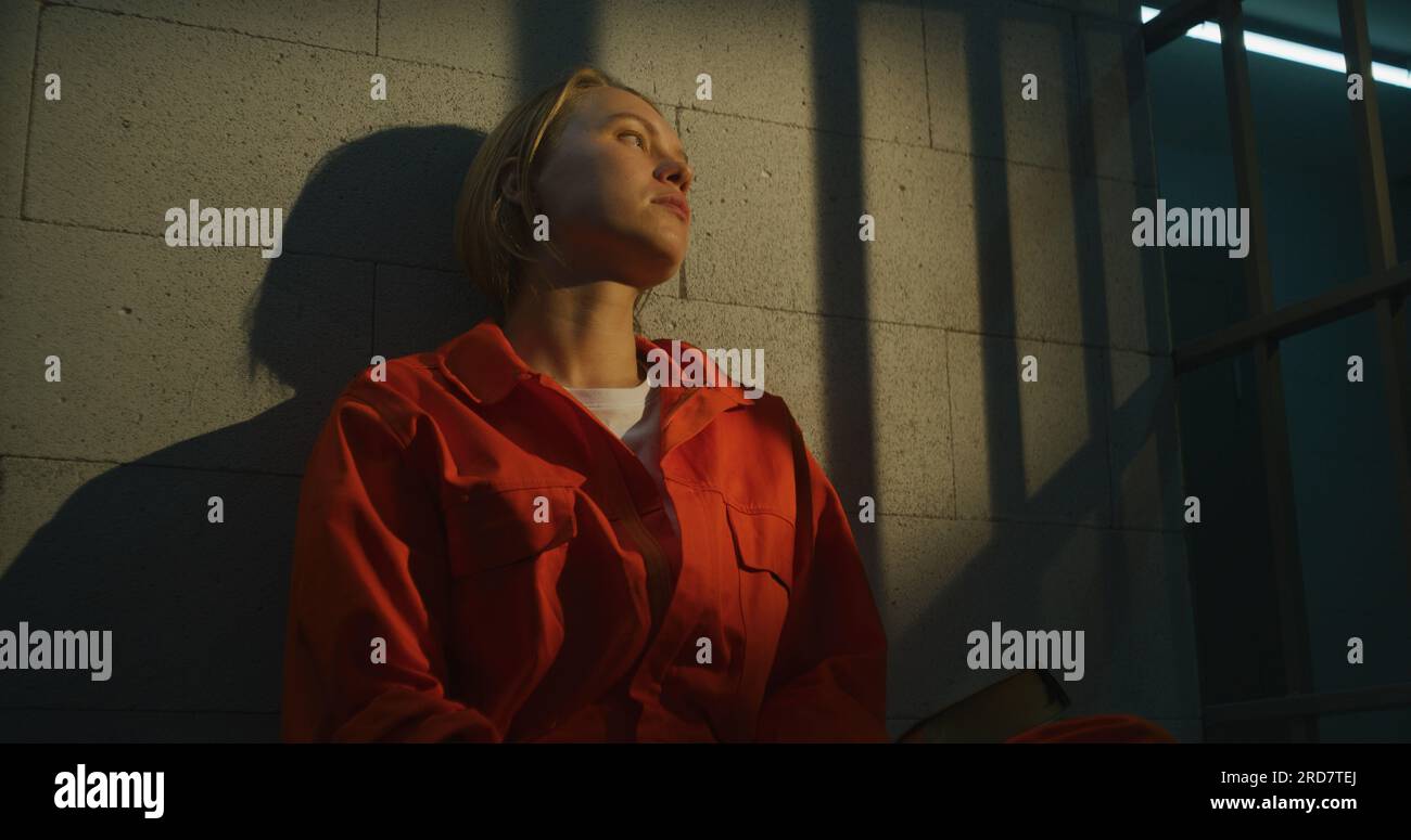 Female prisoner in orange uniform sits on bed in prison cell, reads ...