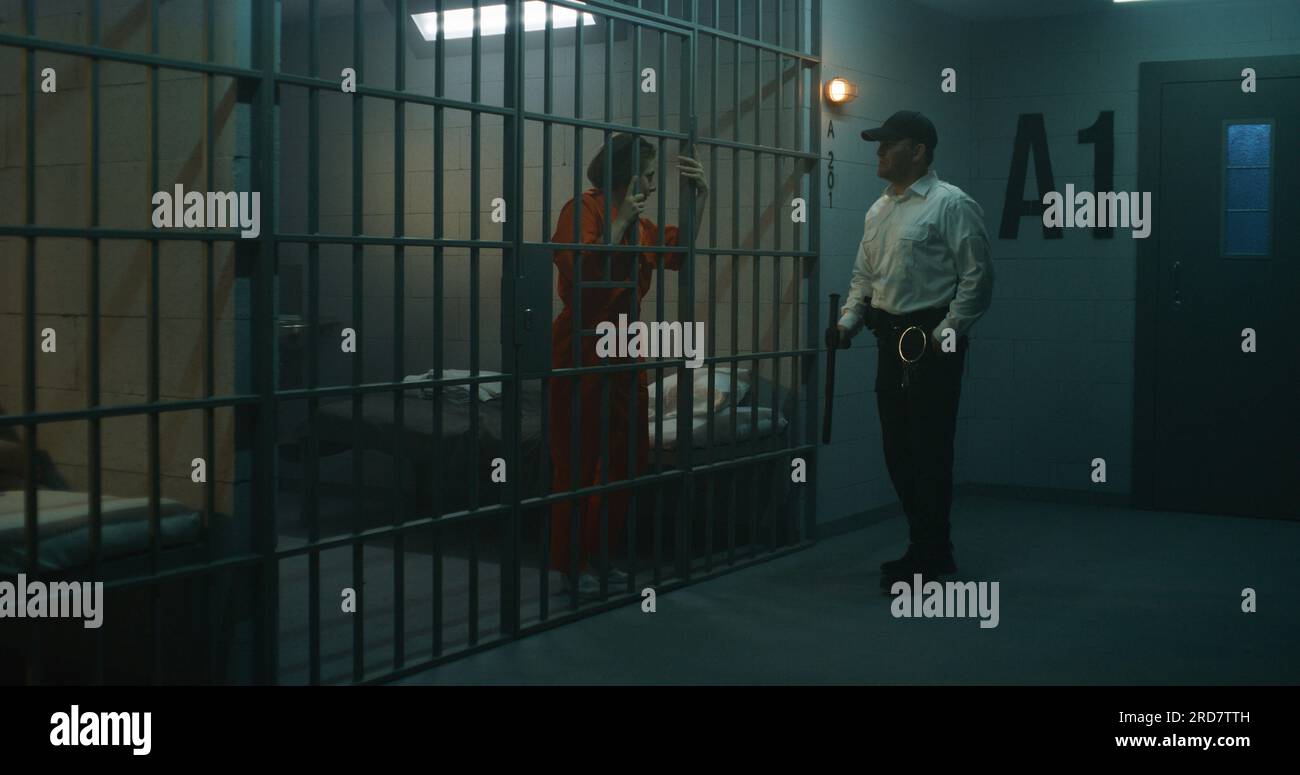 Jailer with police baton stands near prison cell, talks to female ...