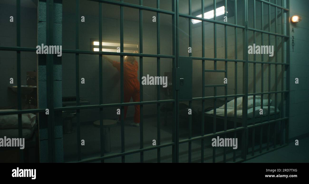 Female prisoner in orange uniform walks and stands behind metal bars ...