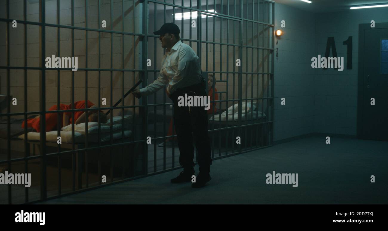 Jailer with police baton stands near prison cell, talks to female ...