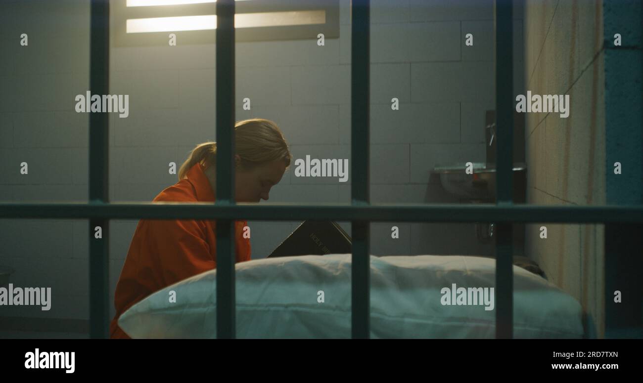 Female prisoner in orange uniform kneels near the bed, prays to God in ...