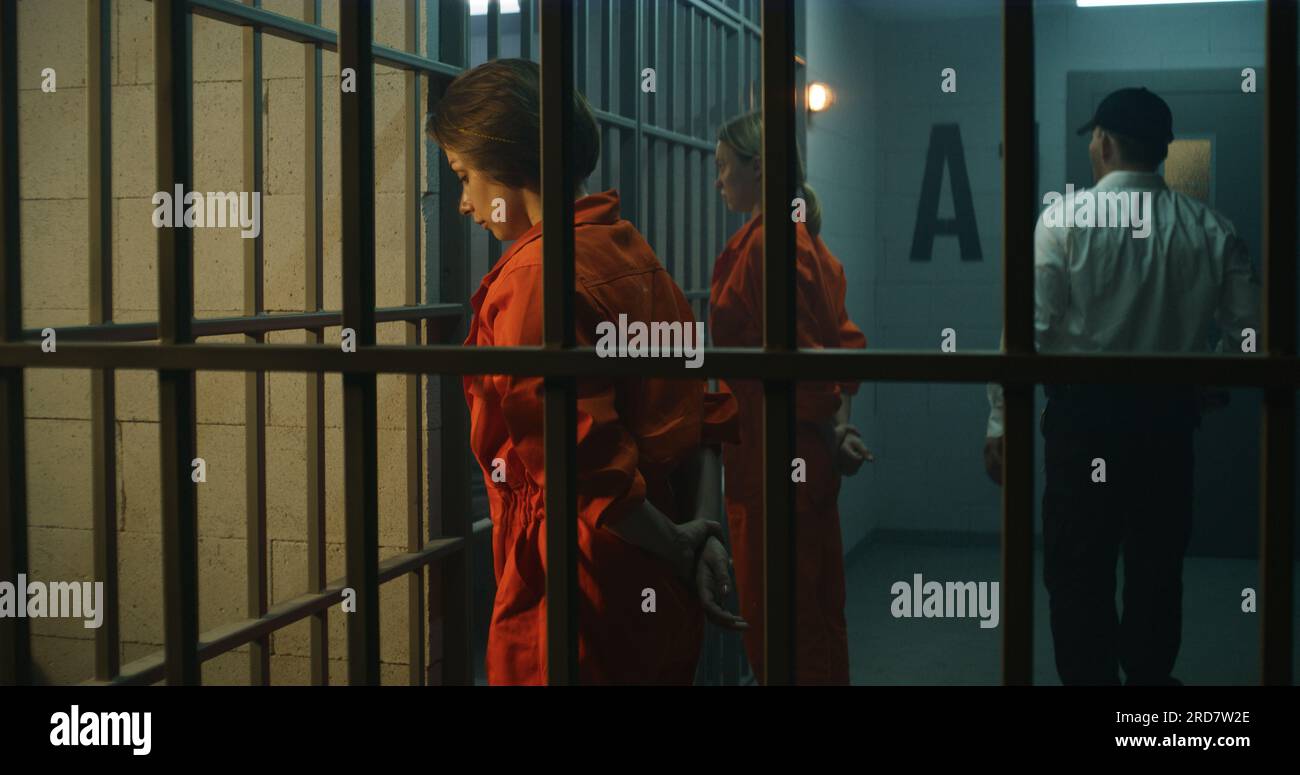 Two female prisoners, inmates in orange uniforms stand facing the metal ...