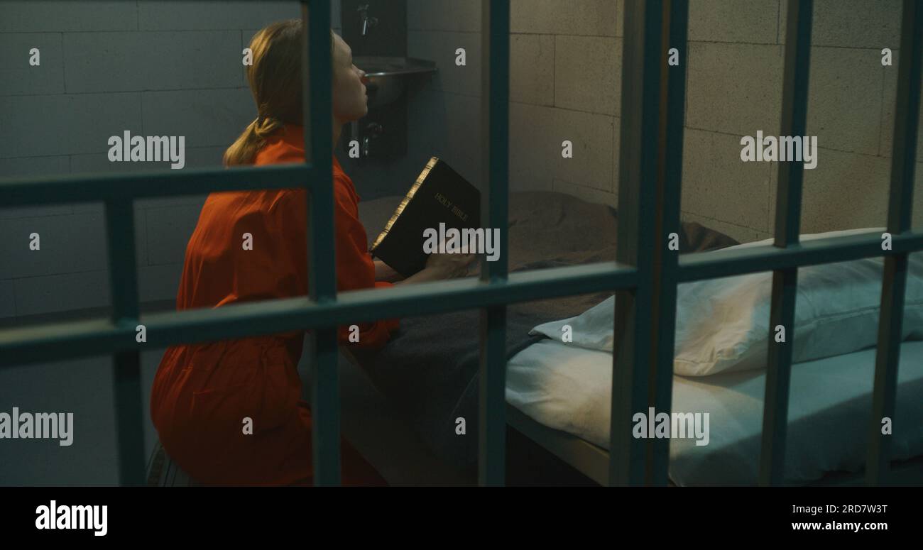 Female prisoner in orange uniform kneels near the bed, prays to God in ...