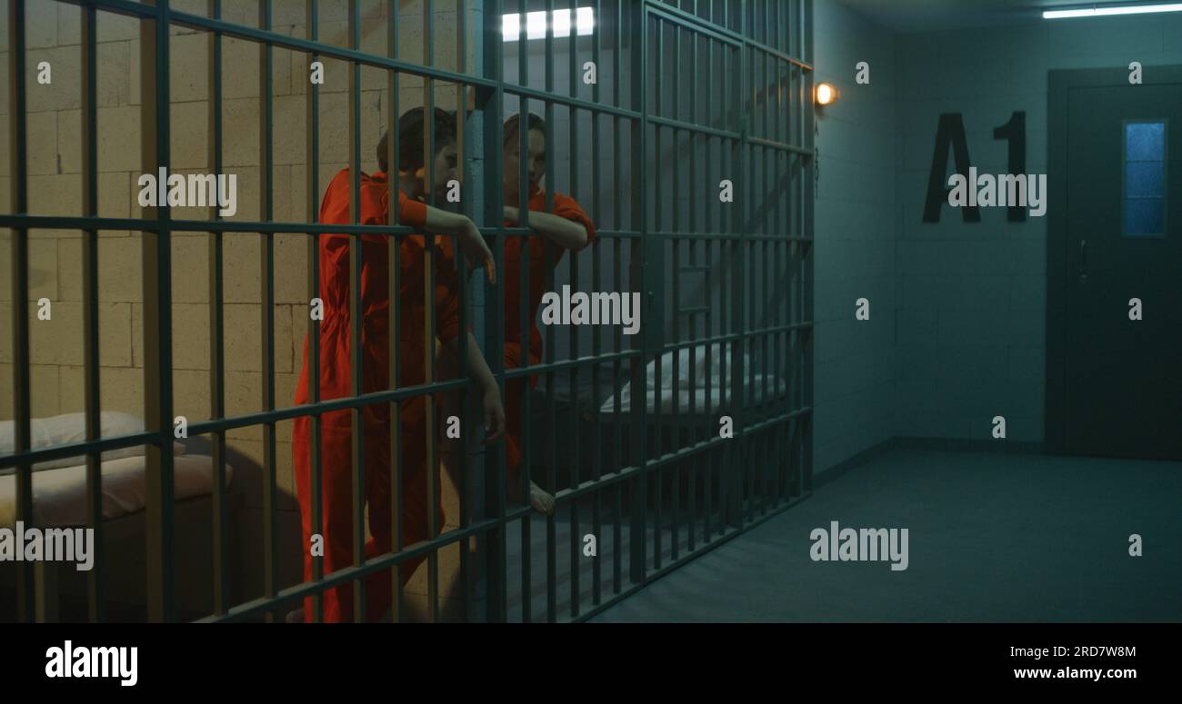 Prison worker walks the corridor. Female prisoners stand behind metal ...