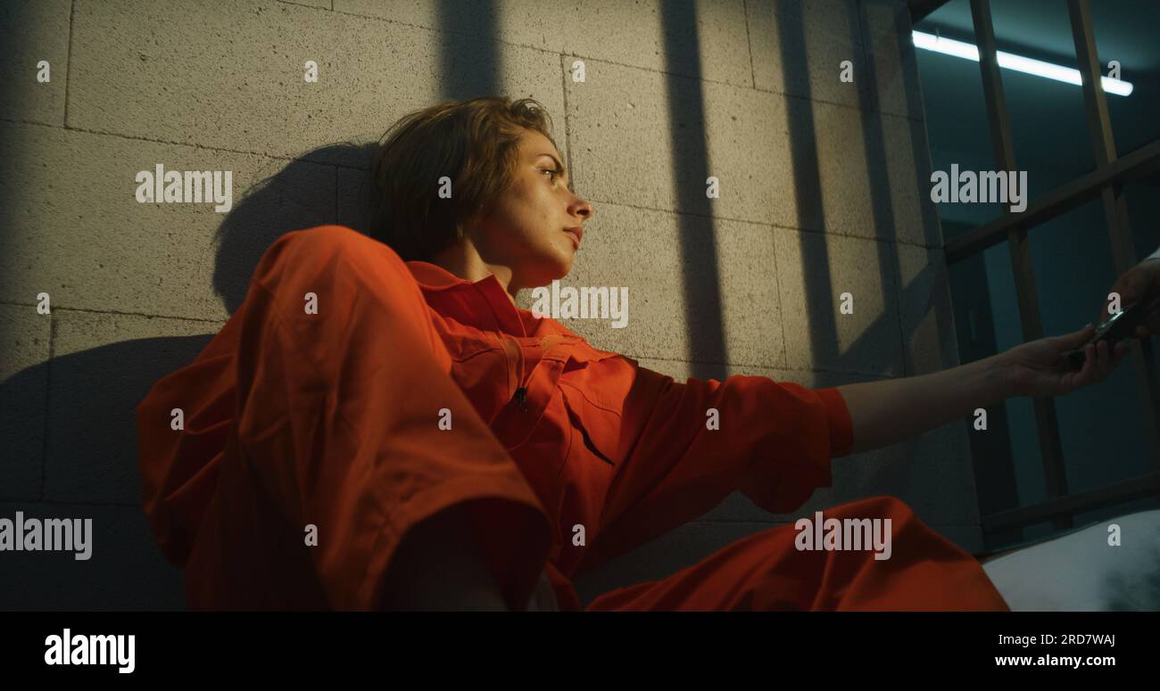 Jailer gives phone to female prisoner. Woman criminal in orange uniform ...