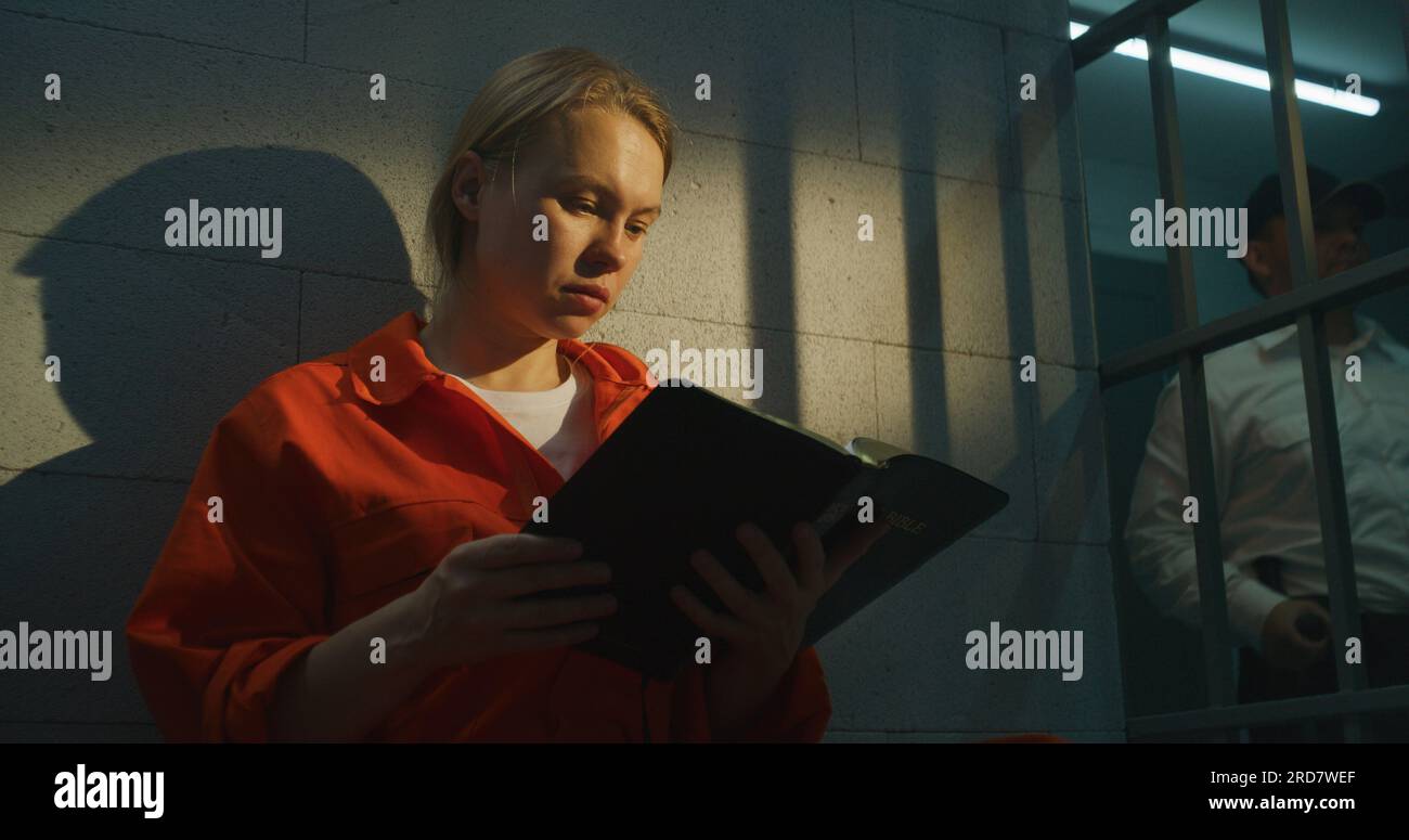 Female prisoner in orange uniform sits on bed in prison cell, reads ...
