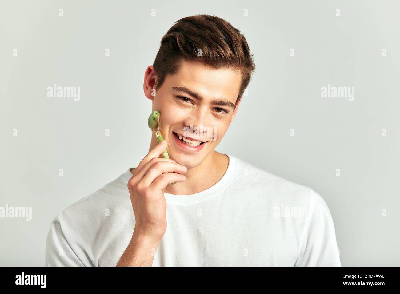 Young handsome smiling brown haired guy using jade de-puffing face ...