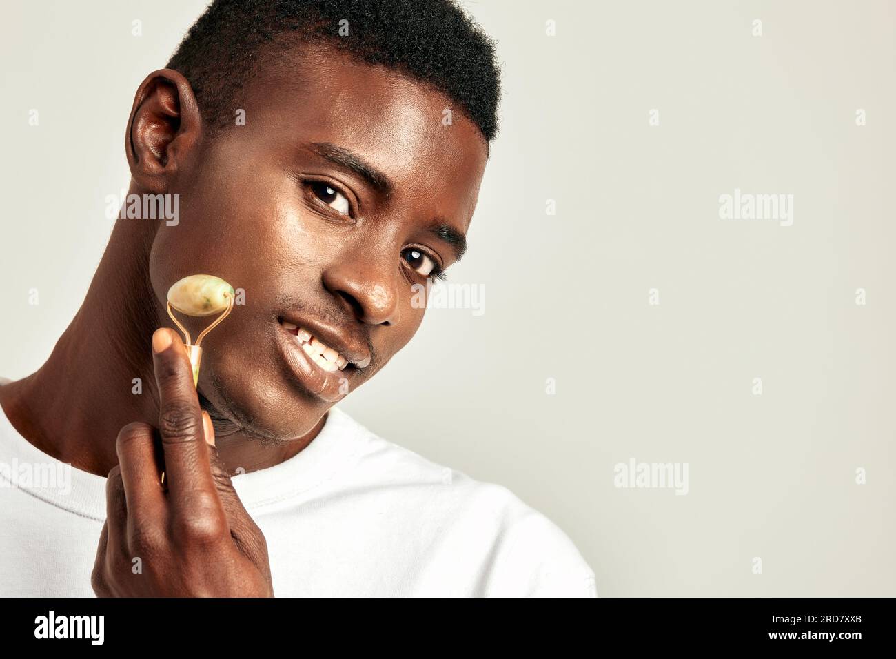 Young handsome black guy using jade de-puffing face roller to keep his ...
