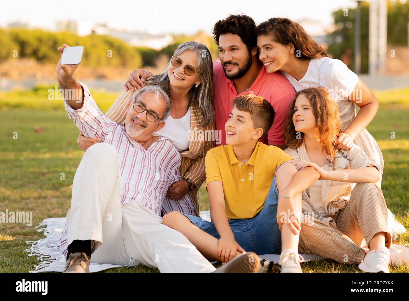 Positive caucasian multi-generation people rest, enjoy picnic in park, take selfie on smartphone ...