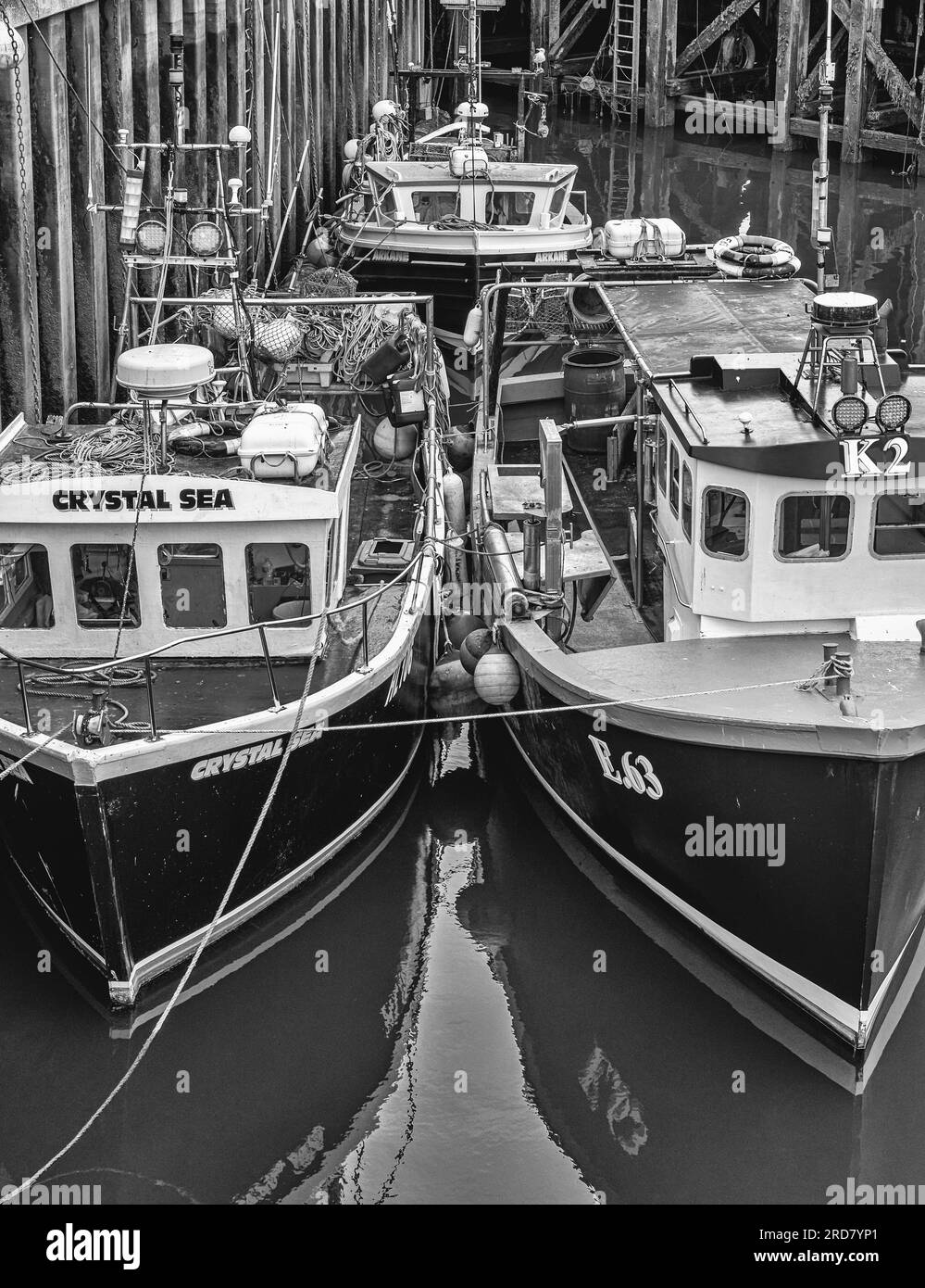 Small fishing boats are reflected in the still waters of a harbour ...