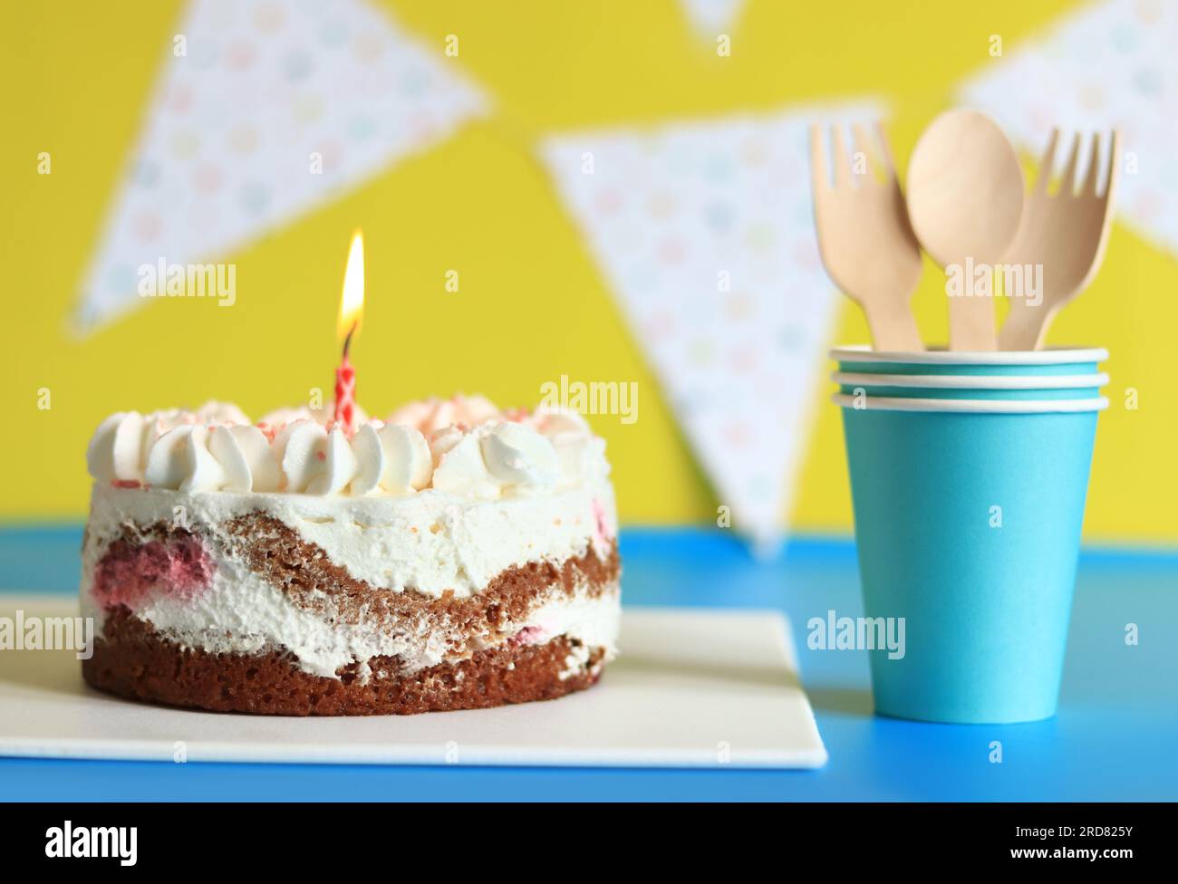 Festive cake with a birthday candle. Cake and paper cup with spoons and ...