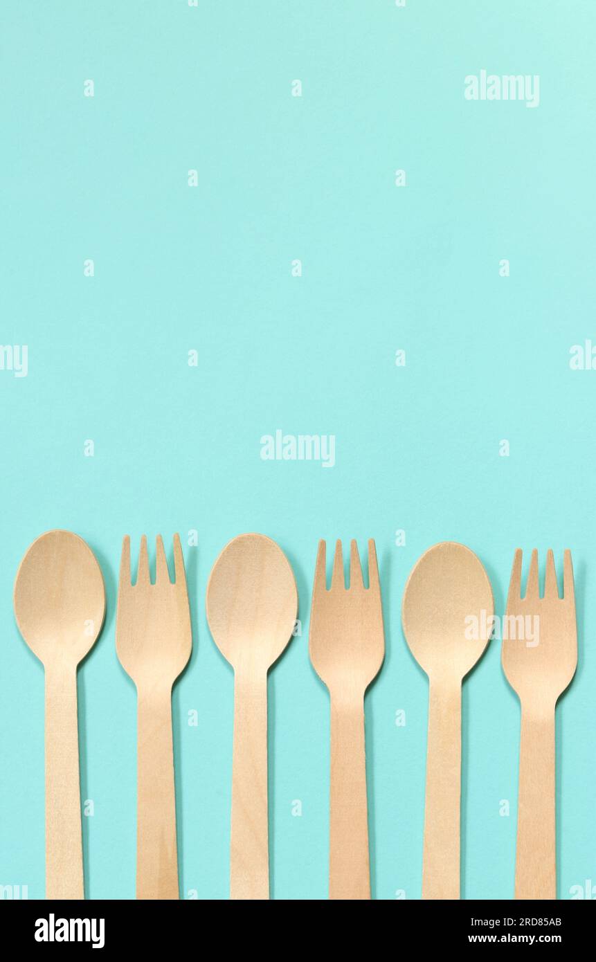 Wooden disposable forks and spoons on a blue background, top view. Eco ...