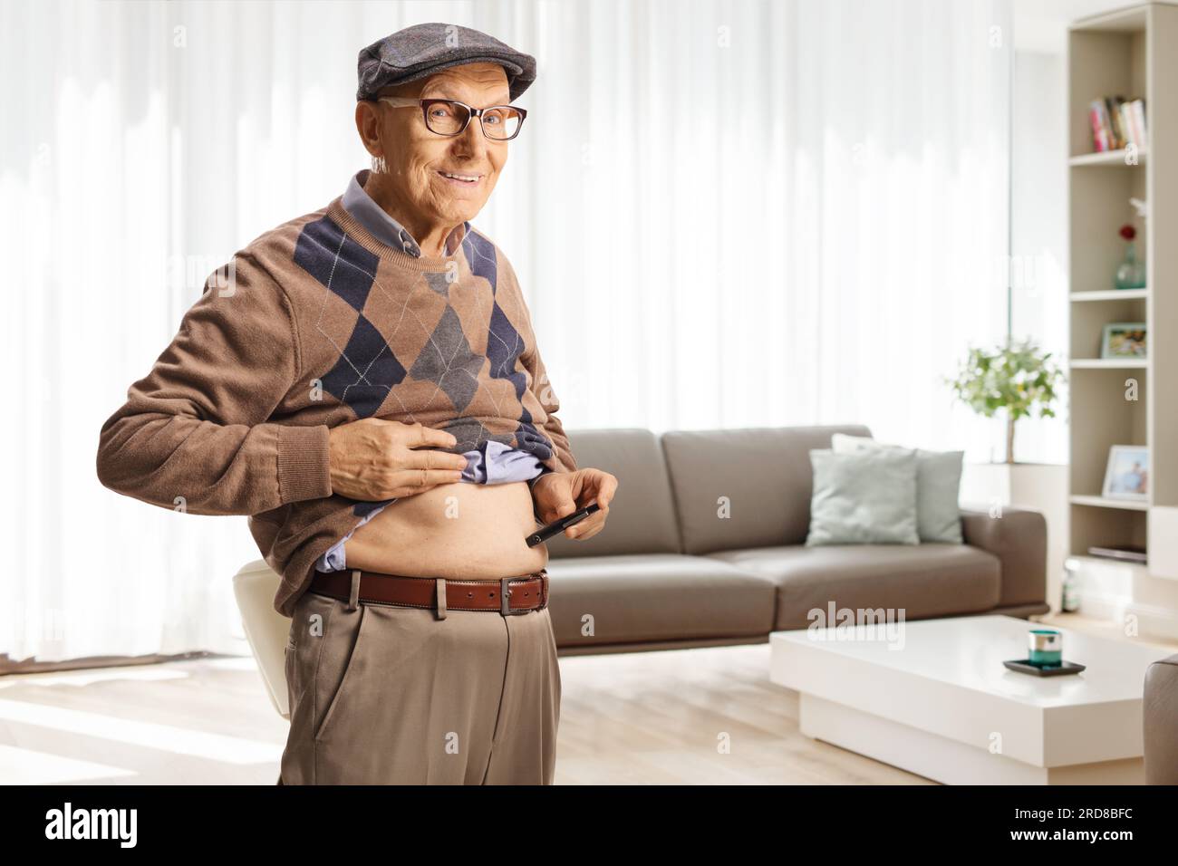 Elderly man poking abdomen with an insulin pen at home in a living room ...