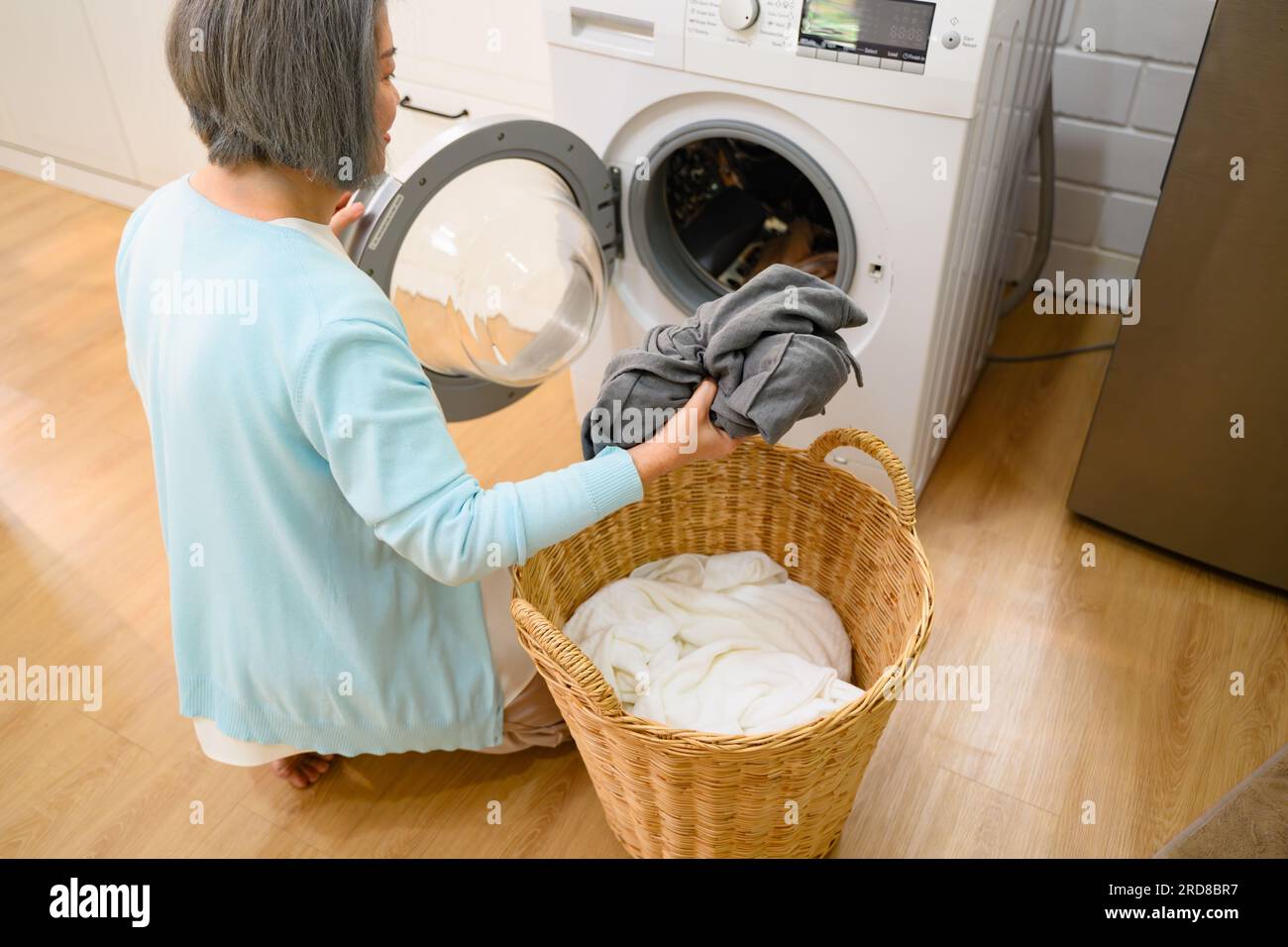 a beautiful senior woman, takes care of the laundry using a washing ...
